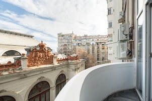 Vista de uma varanda com vista para um edifício histórico com detalhes arquitetônicos elaborados e edifícios modernos ao fundo.