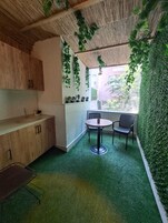 Uma cozinha compacta com armários de madeira, uma mesa redonda com duas cadeiras e um piso de grama sintética verde.