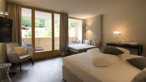 Quarto de hotel com uma cama grande, uma cama menor, um sofá, uma TV e uma varanda com cortinas.