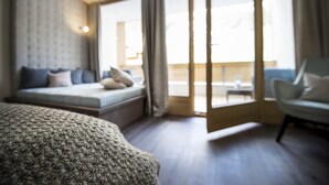 Quarto de hotel moderno com uma cama grande, um sofá e uma cadeira. Há uma porta de vidro deslizante que dá para uma varanda.