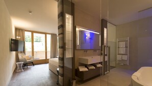 Casa de banho de hotel moderna, com chuveiro envidraçado, uma banheira grande e toucador com espelho.