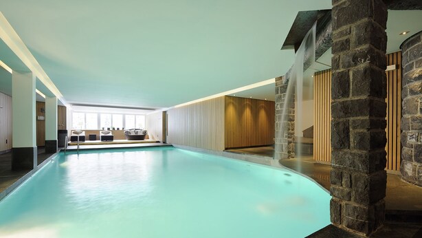 Uma grande piscina interior com paredes de pedra e área de estar com almofadas.