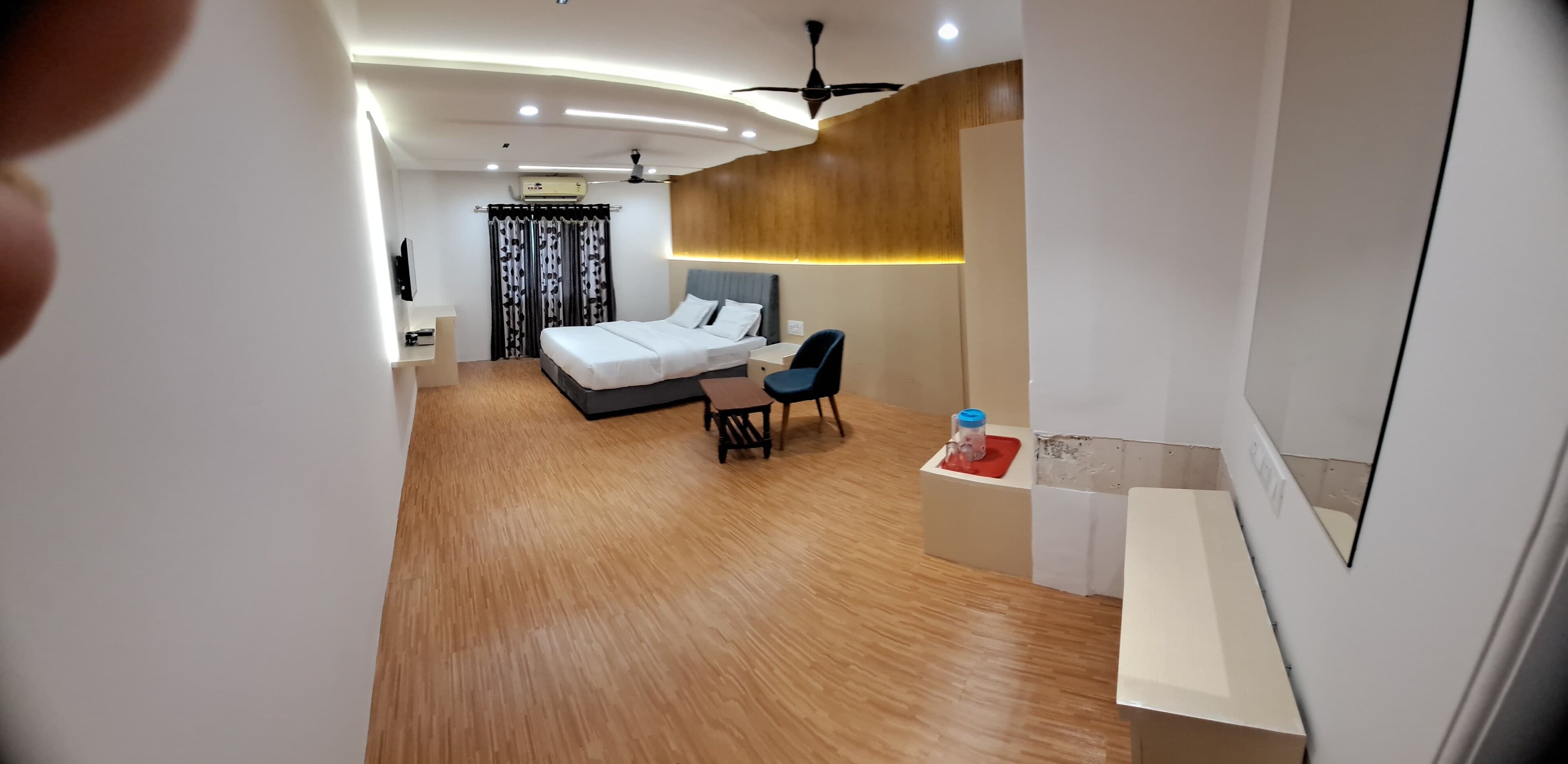 Quarto de hotel moderno com cama, escrivaninha, cadeira e ventoinha no teto.