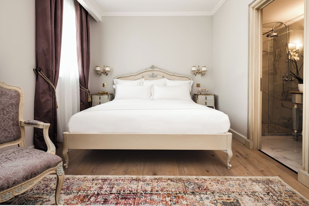 Quarto com cama grande, uma cadeira, mesa de cabeceira e banheiro com chuveiro.