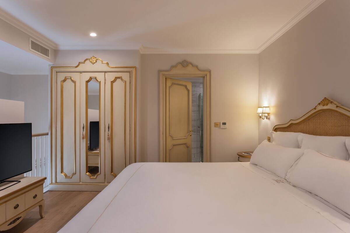 Quarto de hotel com uma cama grande, televisão em uma cômoda, guarda-roupa com espelhos e abajur.