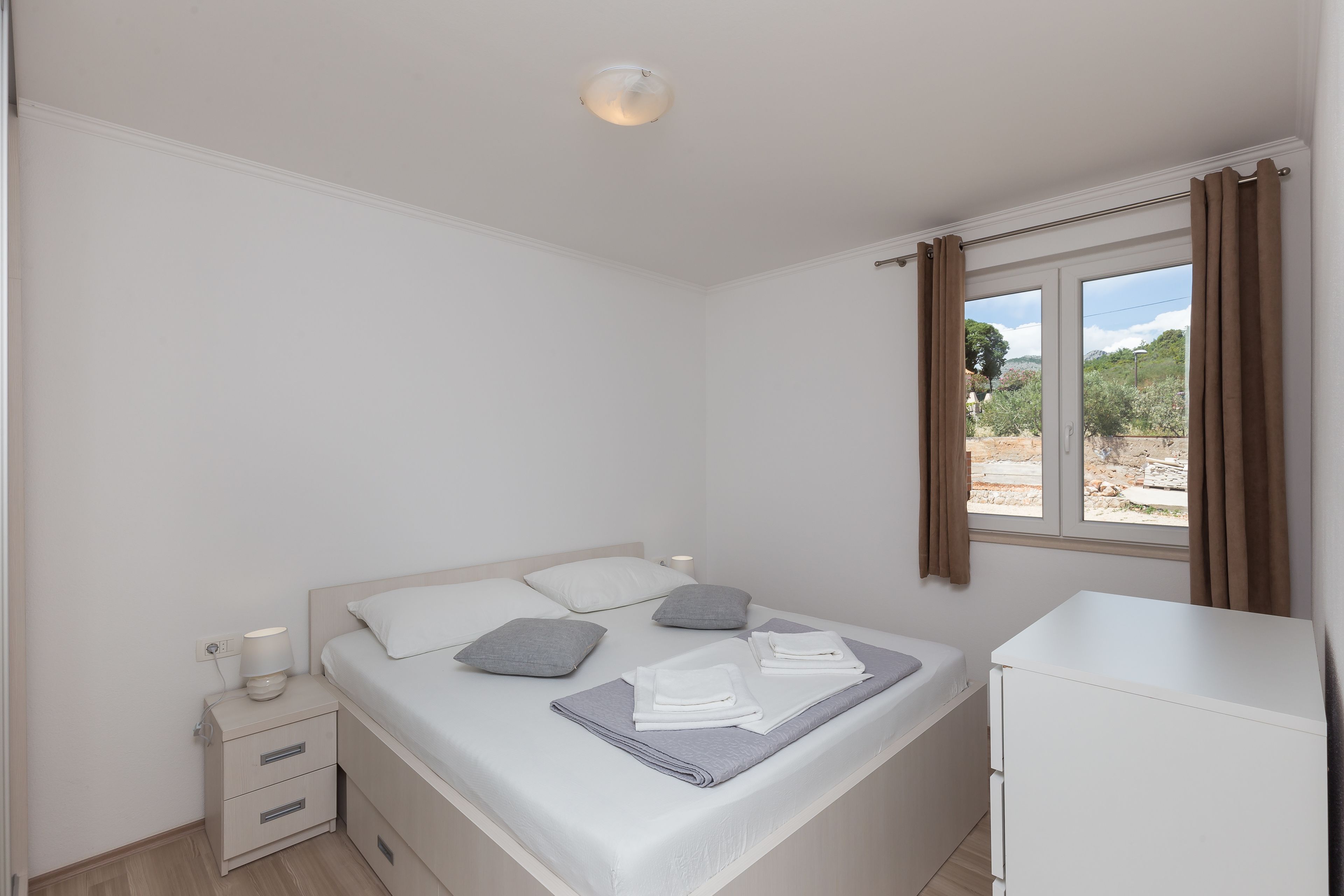 Quarto com cama, mesa de cabeceira, abajur e janela com cortinas.