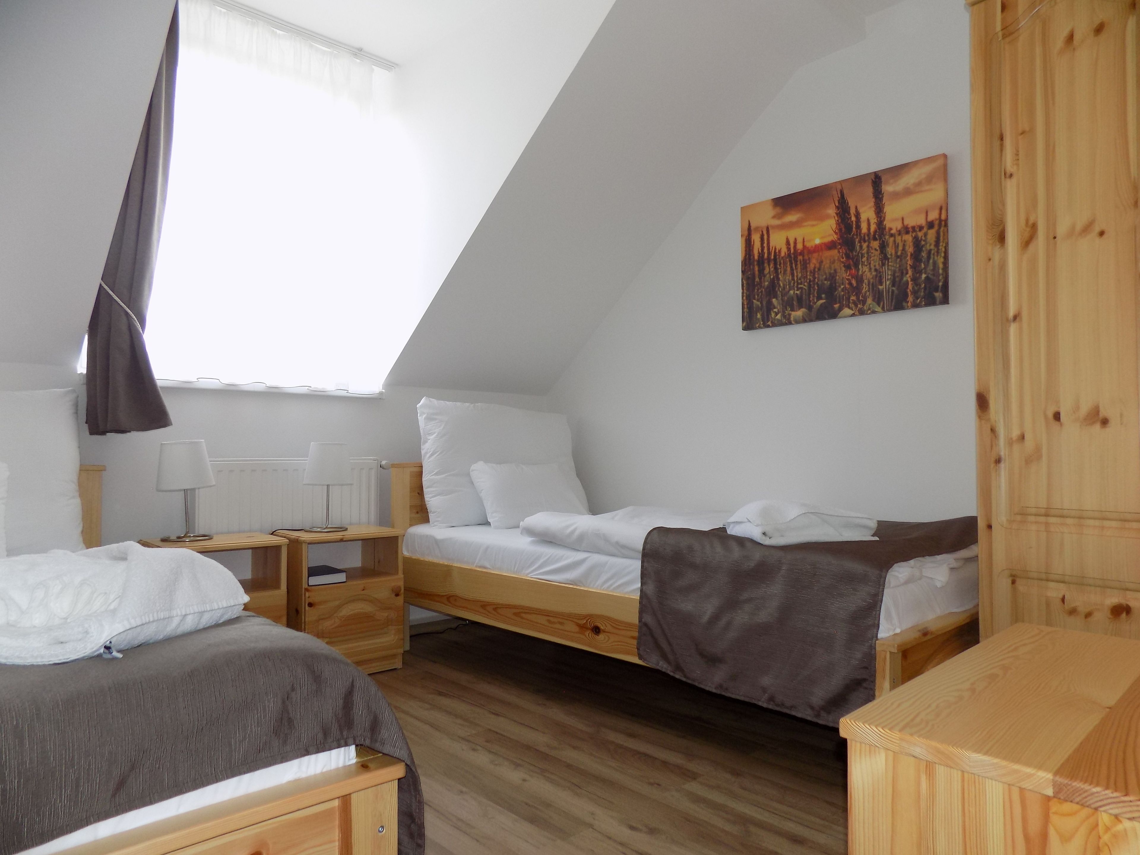 Quarto com duas camas, um guarda-roupa de madeira, um quadro e um claraboia.