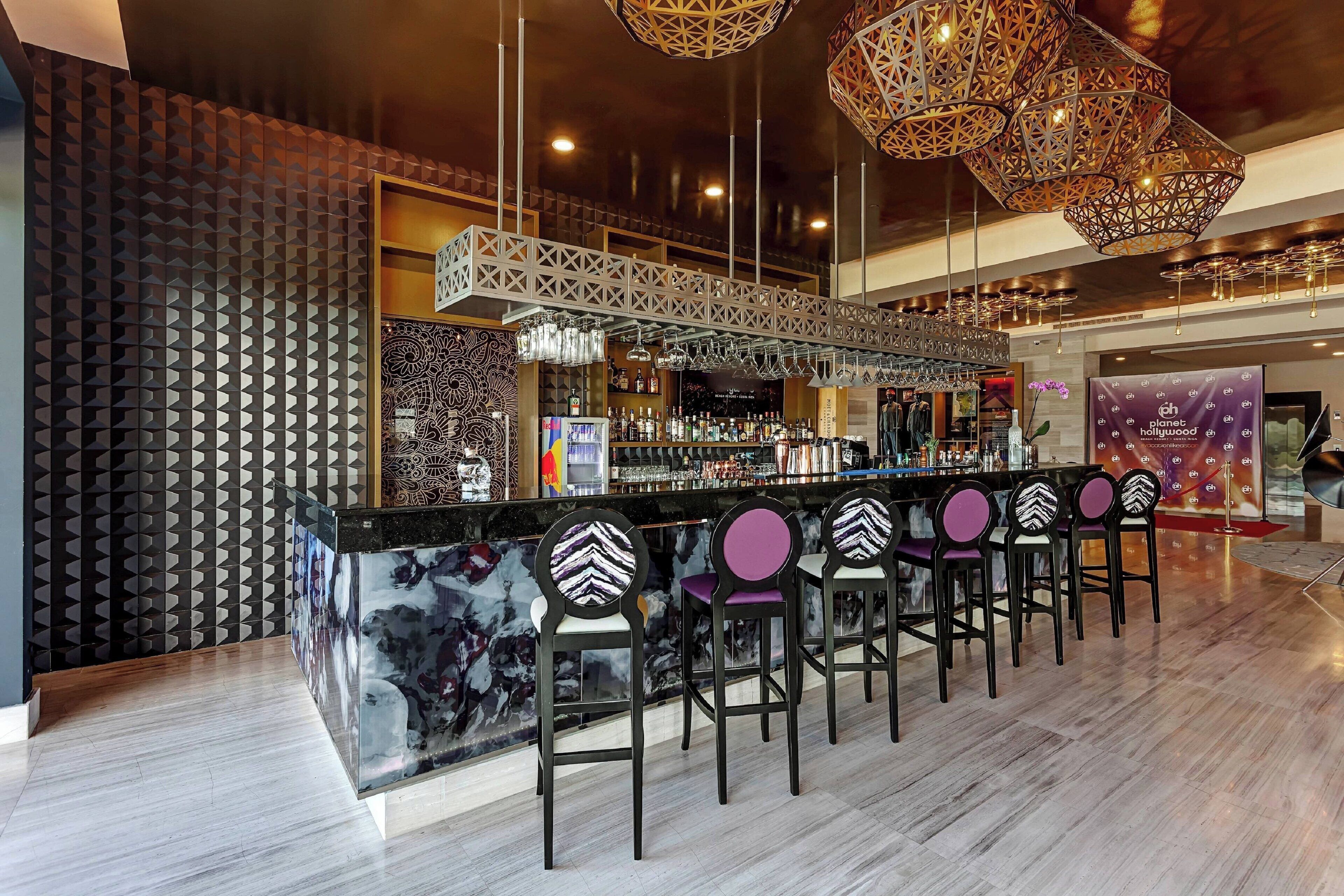 Uma área de bar com design moderno, apresentando uma parede estampada, balcão de mármore e vários bancos.