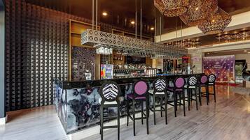 Uma área de bar com design moderno, apresentando uma parede estampada, balcão de mármore e vários bancos.