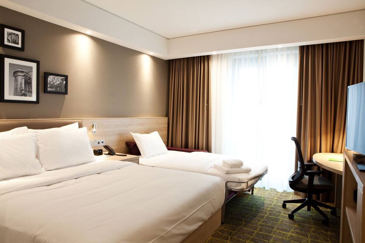 Quarto de hotel com duas camas, uma escrivaninha, uma cadeira e uma televisão.