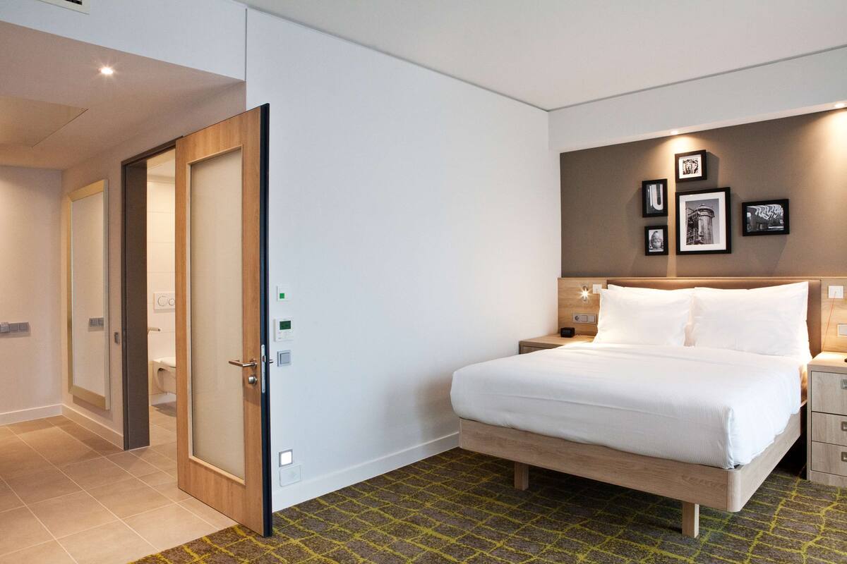 Quarto de hotel moderno com uma cama grande, mesa de cabeceira e uma parede com quadros.
