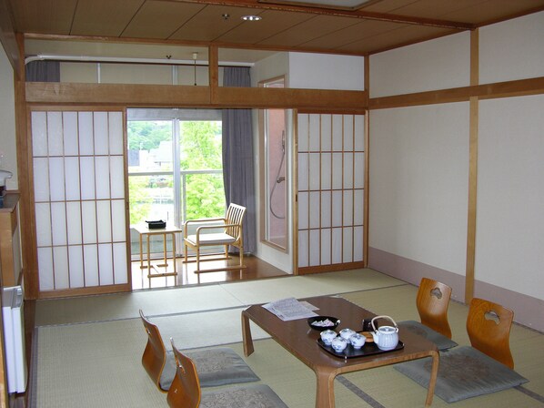 Um quarto japonês tradicional com tatames, uma mesa baixa com conjunto de chá e portas deslizantes que dão para uma área externa.