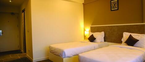 Quarto de hotel com duas camas de solteiro, cabeceira, luminária fixada na parede e porta que dá para outro quarto.