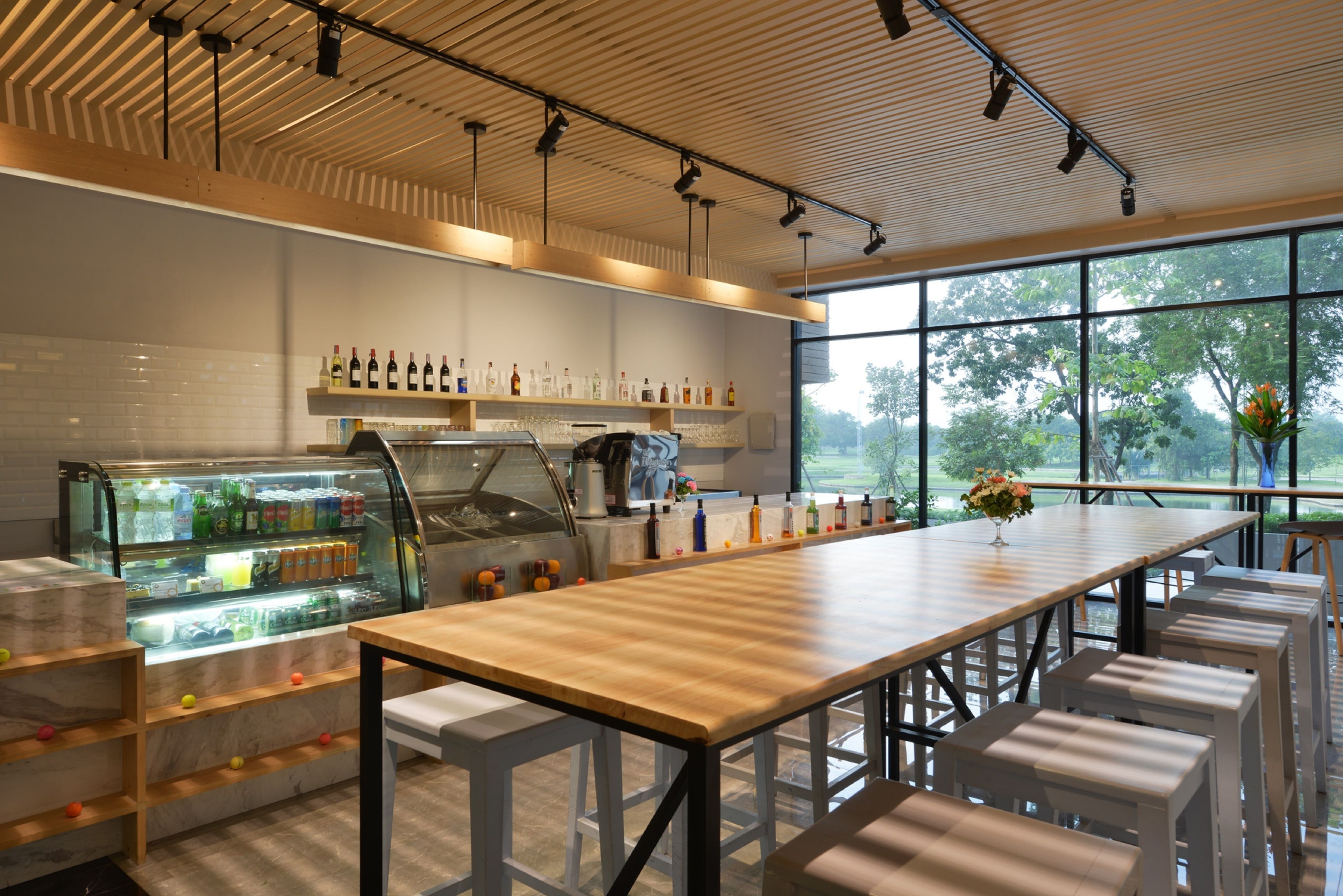 Uma área de bar moderna com um balcão de madeira comprido, banquetas brancas e um refrigerador com bebidas.