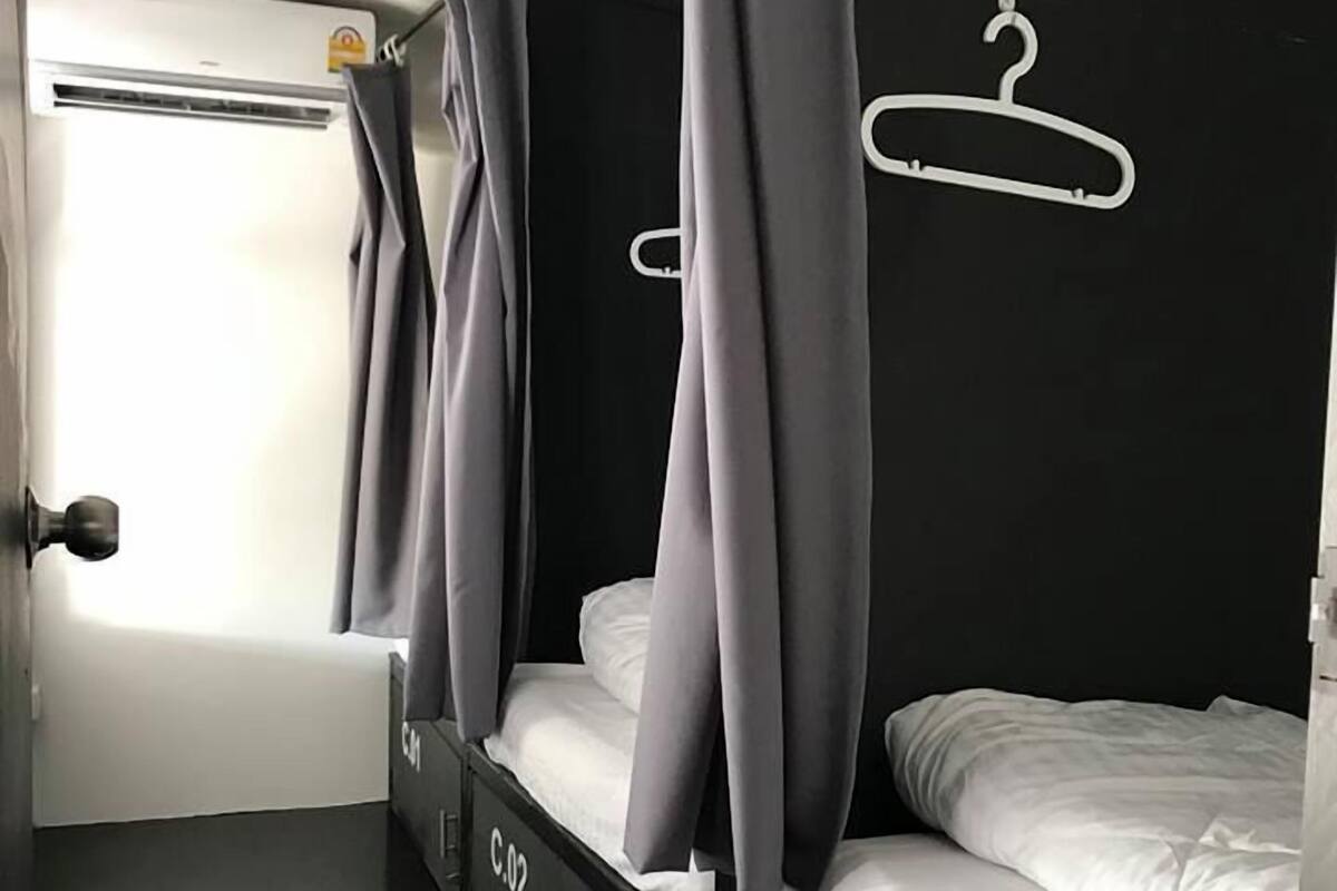 Uma cama de solteiro com dossel, um cabideiro suspenso e uma porta com puxador.