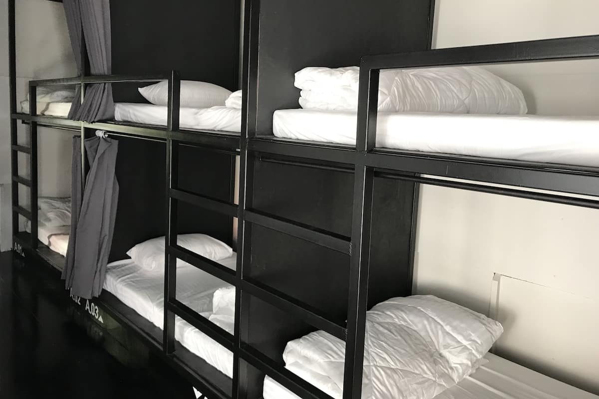 Quarto com beliche, roupa de cama branca e cortina no lado esquerdo.