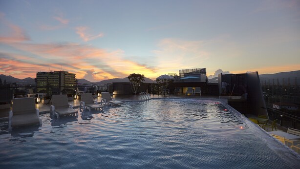 Piscina no terraço com espreguiçadeiras e vista para a cidade ao pôr do sol.