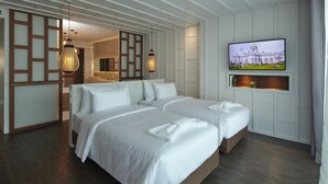 Quarto de hotel com duas camas, televisão presa na parede e banheiro visível através de uma divisória.