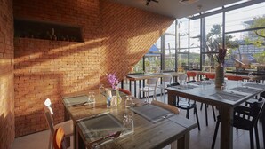 Restaurante com paredes de tijolo, janelas amplas e mesas preparadas para refeições.