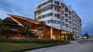 Um hotel moderno de vários andares com telhado plano, grandes janelas e área externa coberta com assentos.