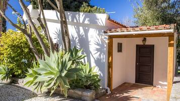 Um pequeno espaço ao ar livre, fechado, com telhado de azulejos, uma porta e uma parede branca.