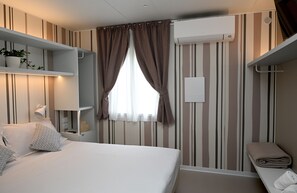 Quarto de hotel com cama, mesa de cabeceira, luminária, ar condicionado e papel de parede listrado.