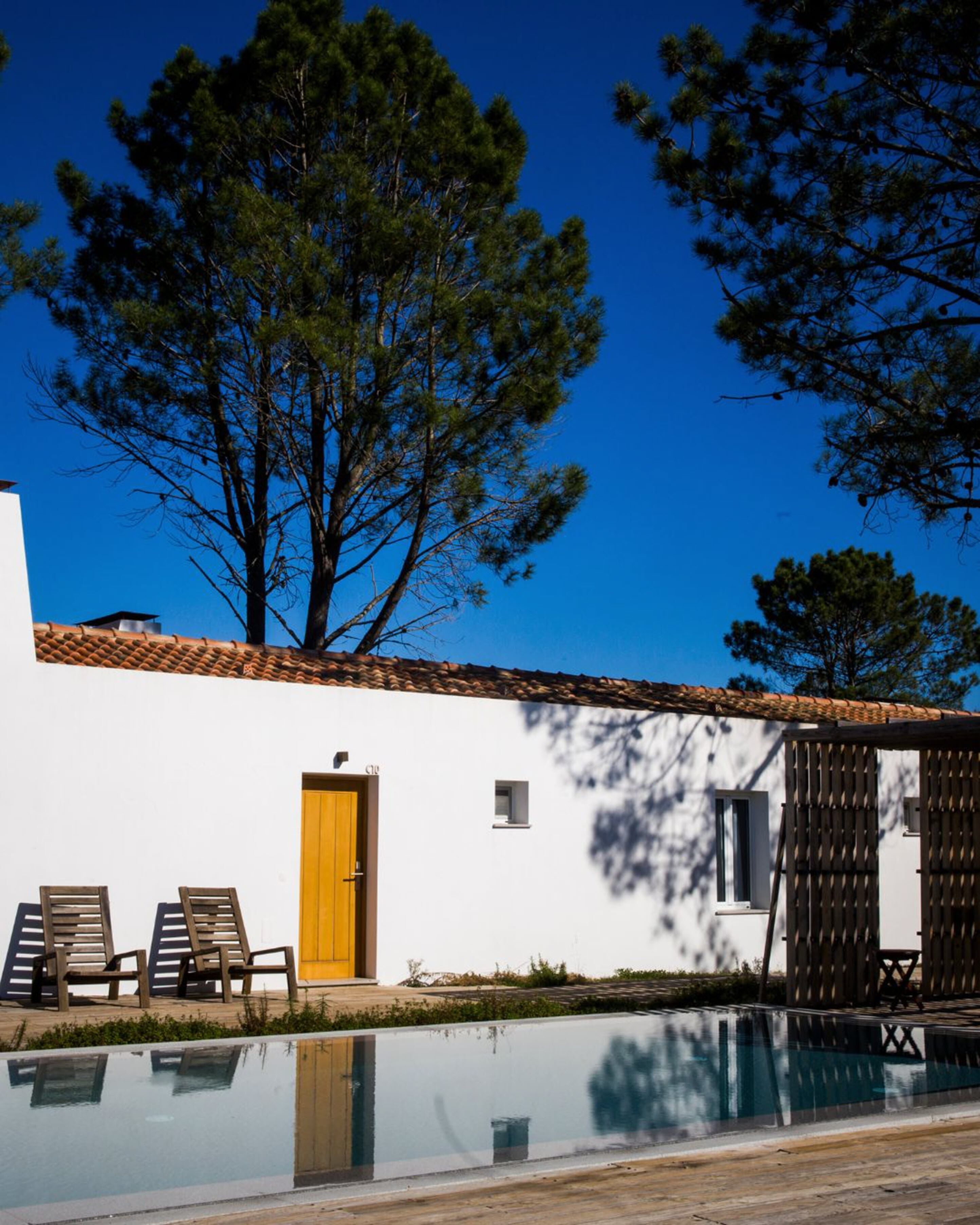 Um edifício branco com telhado de azulejos, piscina e duas espreguiçadeiras.