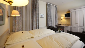 Quarto de hotel com uma cama grande, duas mesas de cabeceira, uma escrivaninha com cadeira, uma televisão e um guarda-roupa.