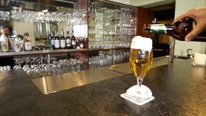 Um bar com um copo de cerveja em um apoio, uma mão servindo cerveja no copo e um espelho refletindo o balcão.