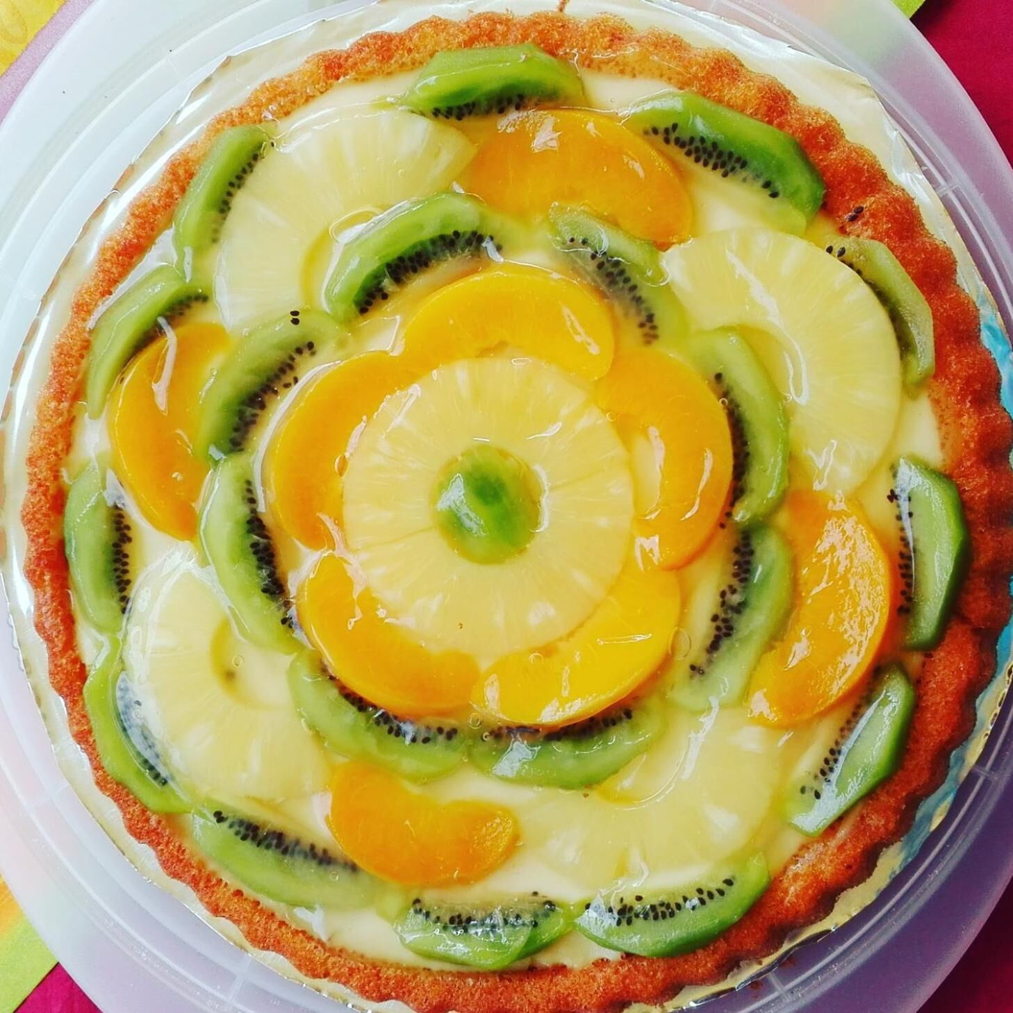 Uma tarte de frutas com crosta dourada, coberta com fatias de kiwi, abacaxi e laranja.