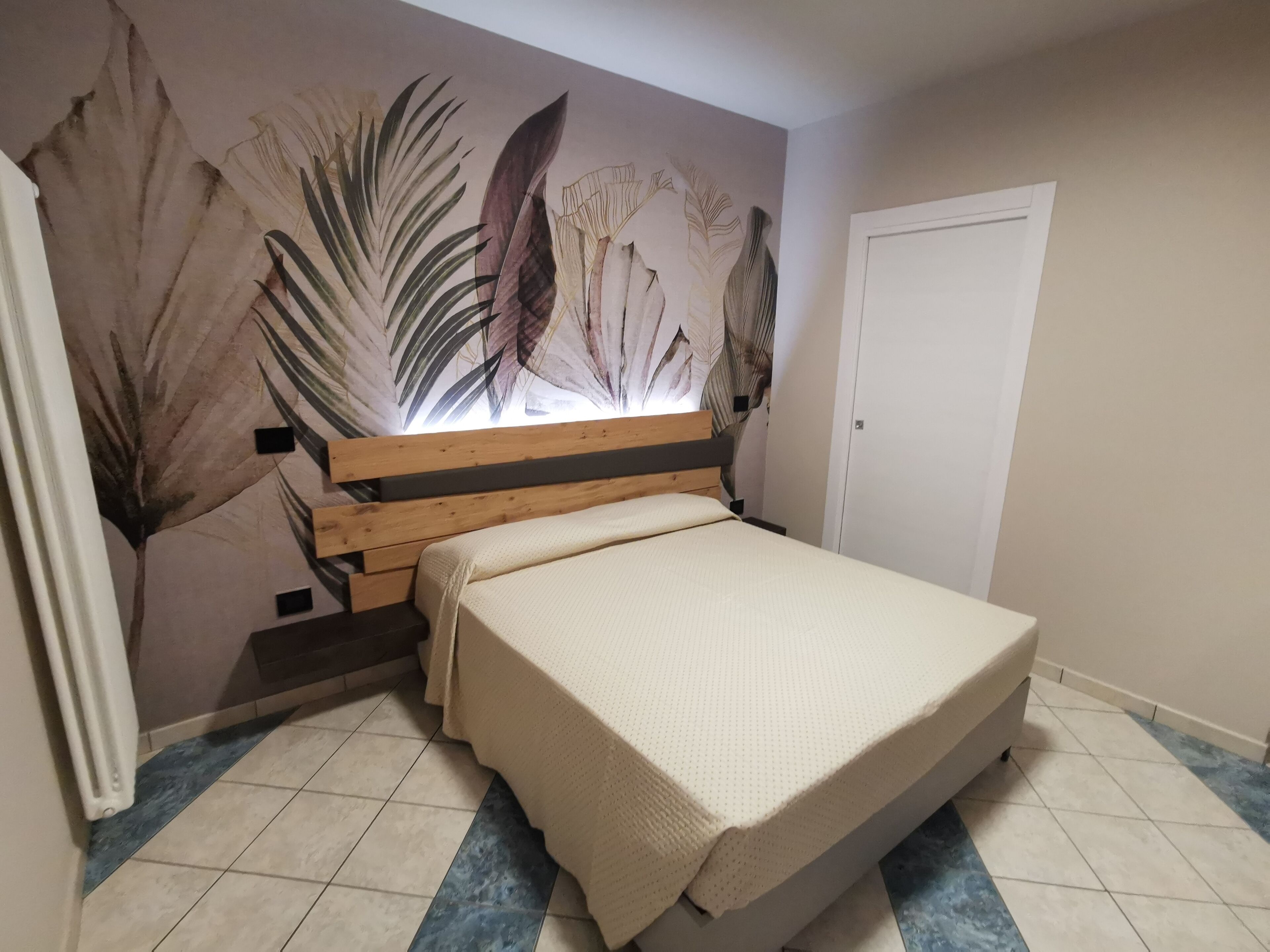 Quarto com cama, cabeceira de madeira, painel na parede e porta.