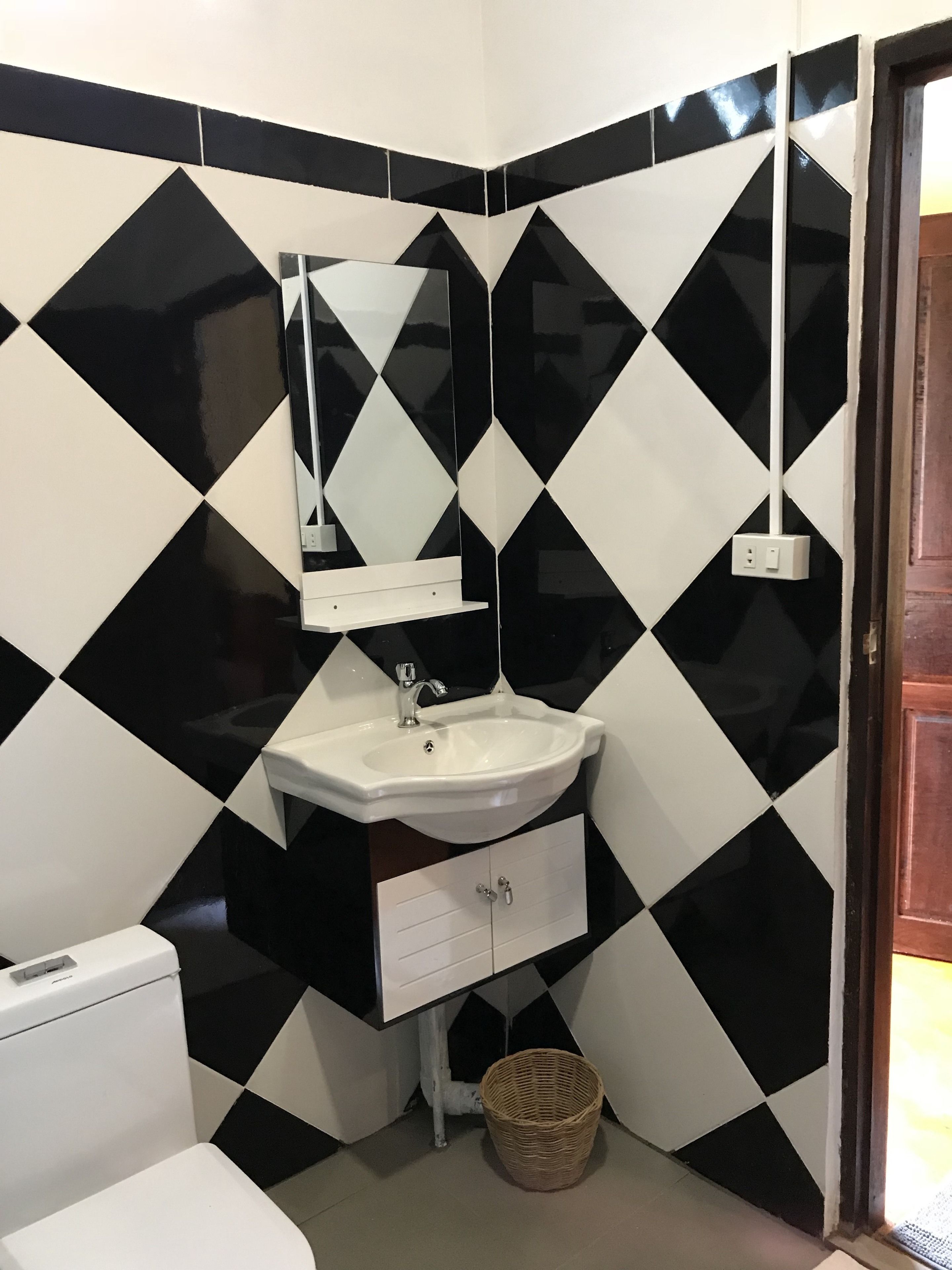 Um banheiro com piso quadriculado em preto e branco, uma pia branca com espelho acima e um vaso sanitário branco.
