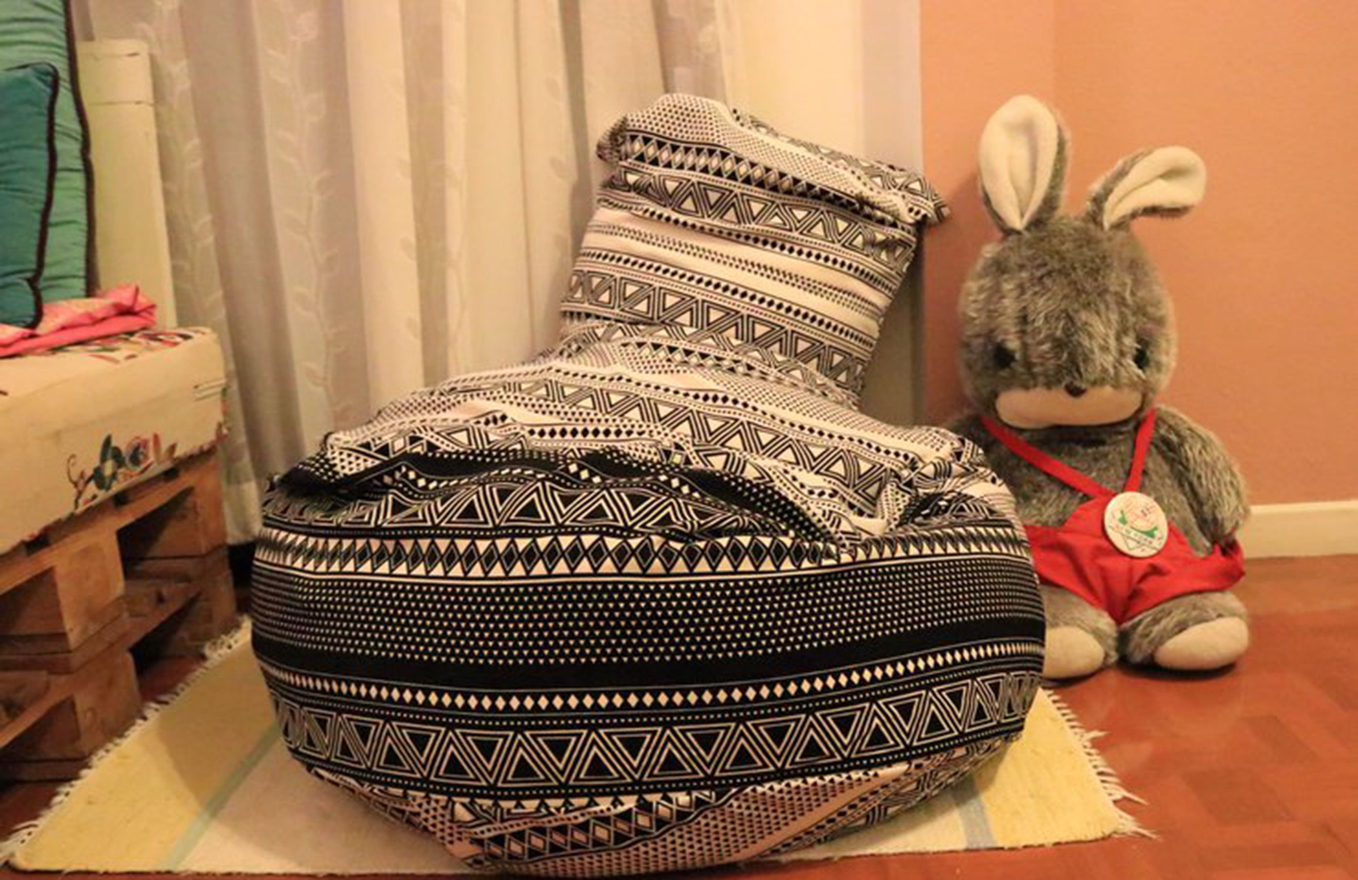 Uma cama com um cobertor estampado e almofadas, um brinquedo de pelúcia e um palete de madeira.