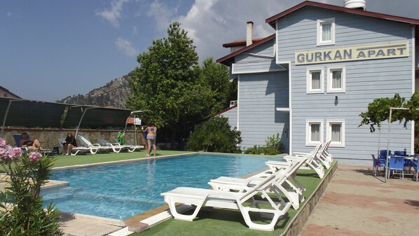 Uma área de piscina com espreguiçadeiras e um edifício com a inscrição "GURKAN APART".