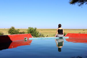 Uma pessoa sentada na beira de uma piscina infinita com telhas vermelhas, apreciando a vista do horizonte.
