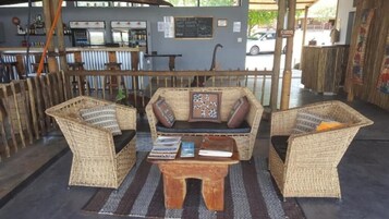 Uma área de estar rústica ao ar livre, com móveis de vime e uma pequena mesa de madeira, cercada por um portão de madeira.