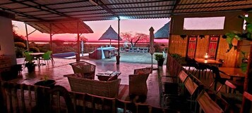 Área de estar externa com mobiliário de vime e um bar, com vista para uma paisagem deslumbrante.