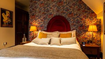 Cama bem arrumada com cabeceira vermelha, duas mesas de cabeceira com abajures e papel de parede floral.