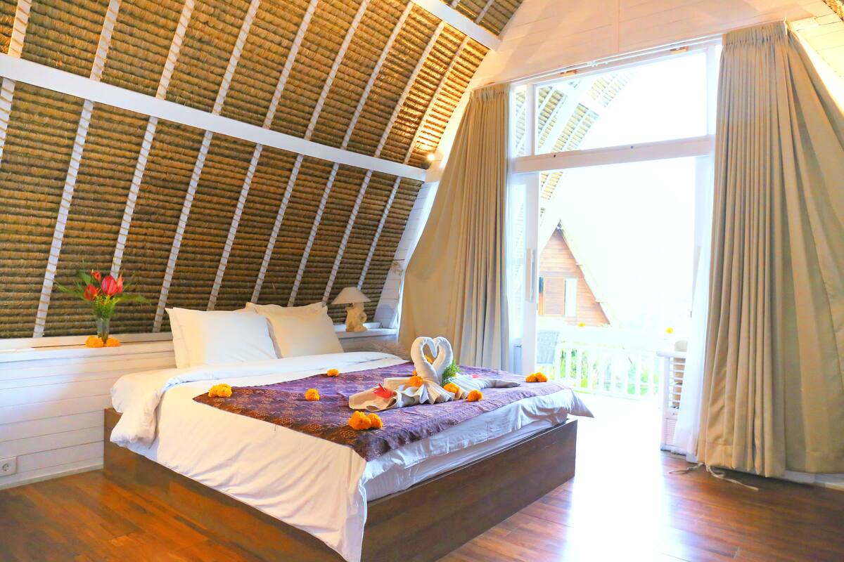 Quarto com uma cama grande, janela com cortinas e vista para o exterior, além de teto de madeira.