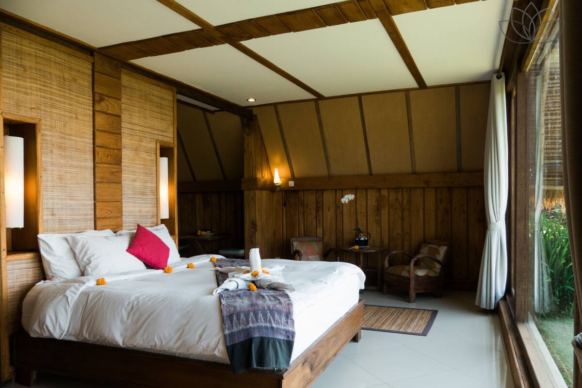 Um quarto espaçoso com uma cama grande, vigas de madeira, uma mesinha e uma cadeira.