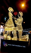 Uma escultura iluminada de um homem fazendo um pedido a uma mulher, com um balão em forma de coração.