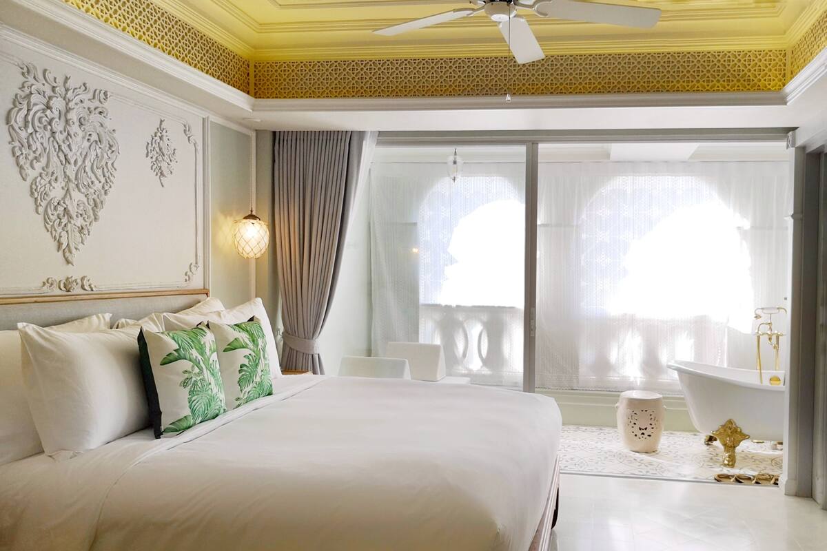 Um quarto espaçoso com uma cama grande, ventilador de teto e vista para a varanda através de cortinas leves.