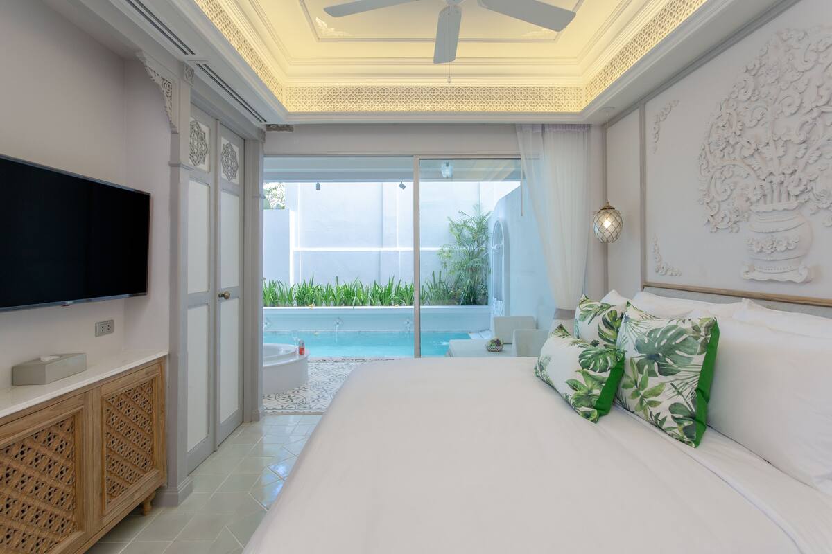 Quarto com uma cama grande, televisão de tela plana, ventilador de teto e vista para uma piscina.