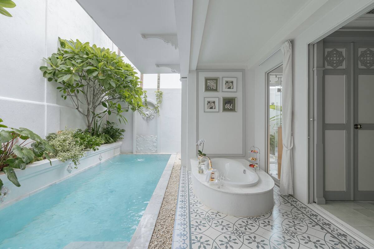 Área de piscina privativa com hidromassagem, cercada por plantas e piso cerâmico.