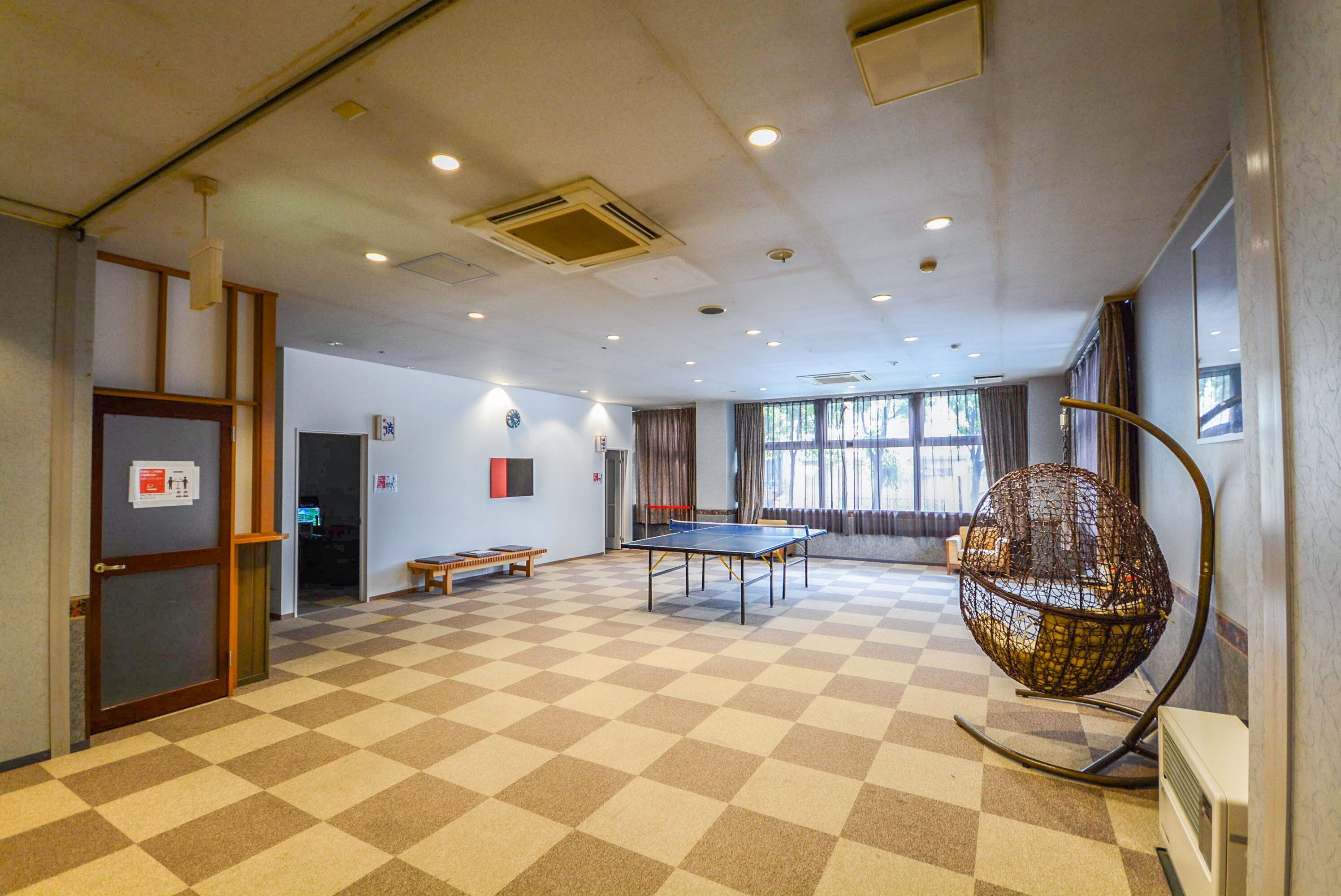 Um quarto espaçoso com piso xadrez, mesa de pingue-pongue, área de estar e uma grande janela com cortinas.