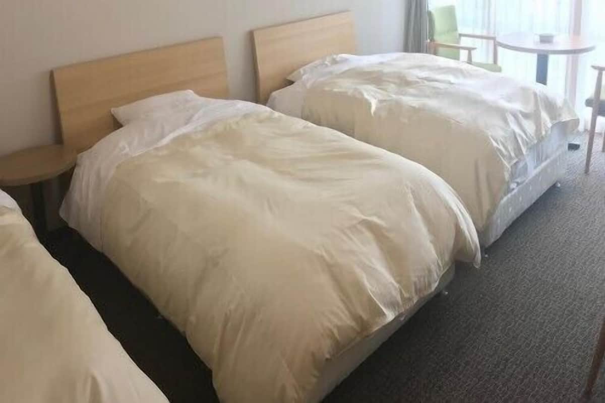 Quarto de hotel com duas camas, uma mesinha e uma cadeira.