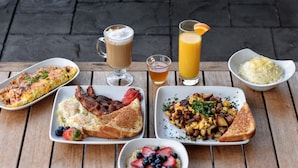 Uma mesa de madeira com itens de café da manhã, como torradas, ovos, bacon e uma tigela de frutas.