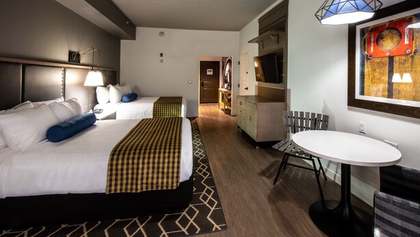 Quarto de hotel com duas camas, uma escrivaninha, uma cadeira, uma televisão e uma mesa pequena.