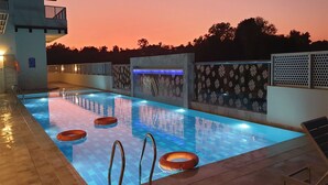 Piscina com água azul cristalina, rodeada por piso cerâmico e equipada com corrimãos de metal.