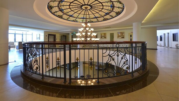 Um hall espaçoso com uma balaústres circulares no centro, teto em vitrais e um lustre.